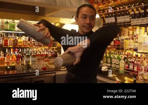Smiling Asian smart bartender shaking with two hands in mixed cocktail ...