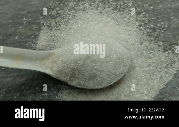 white granulated sugar. granulated sugar on a white spoon made of ...