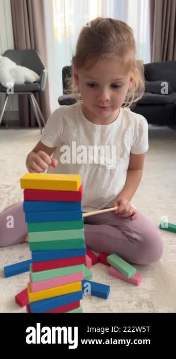 Little girl playing board game at home, taking colorful blocks from wooden tower. vertical video ...