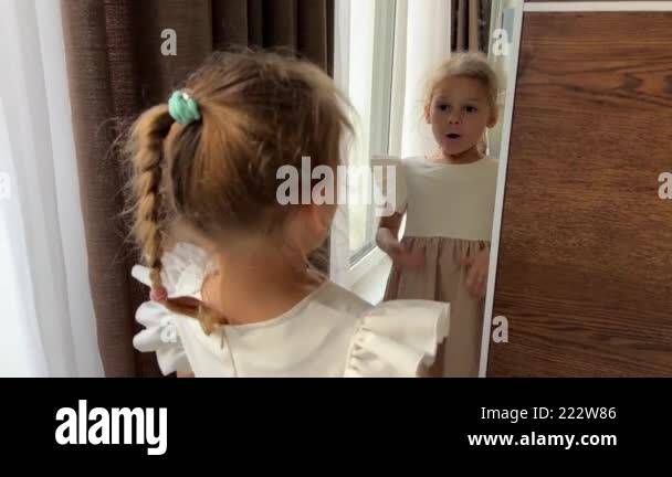 Little girl in dress preening in front of the mirror in home bedroom ...