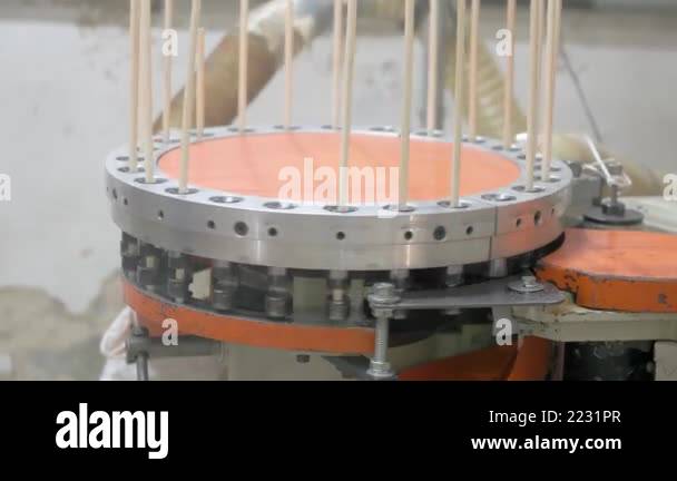 A machine processes wooden dowels, arranging them vertically in a ...