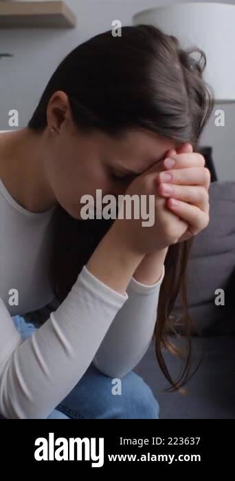 Vertical video of anxious sad young woman sitting on couch, worrying ...