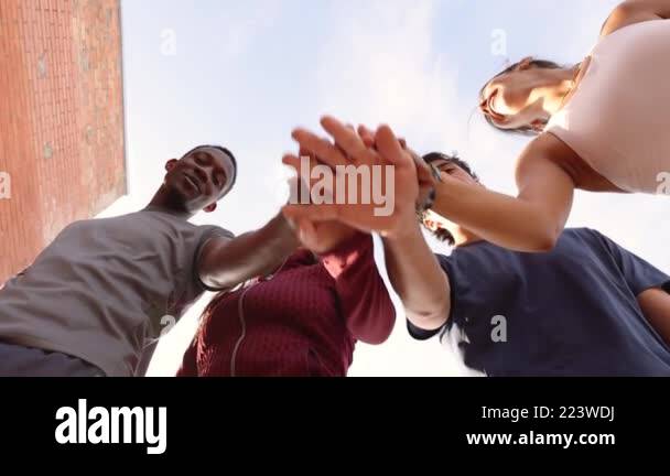 Low-angle shot of a diverse group of friends cheerfully joining their hands together ...