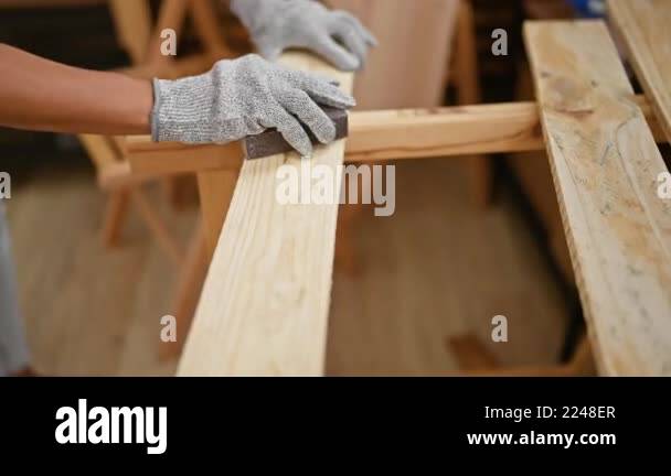 Hispanic woman carpenter at work, sanding wood plank with her hands at ...