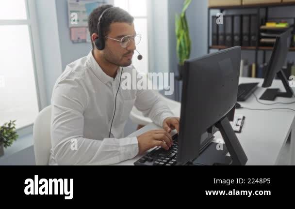 Young man wearing headset working at computer in modern office ...