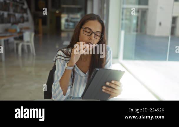 Woman reading tablet in a modern office, looking frustrated as sunlight ...