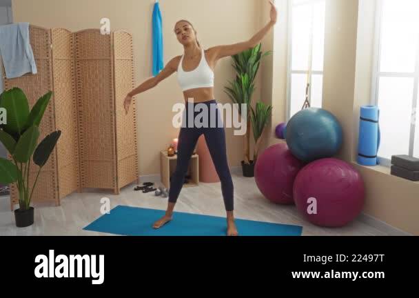 Young woman stretching in a gym with exercise balls, yoga mat, wooden ...