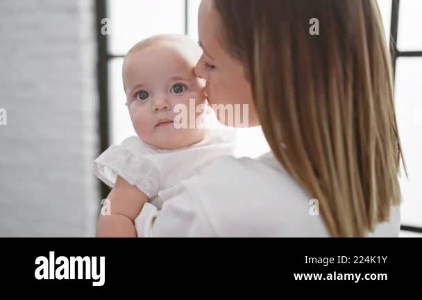 Casual and relaxed, a mother is standing, lovingly holding her baby ...