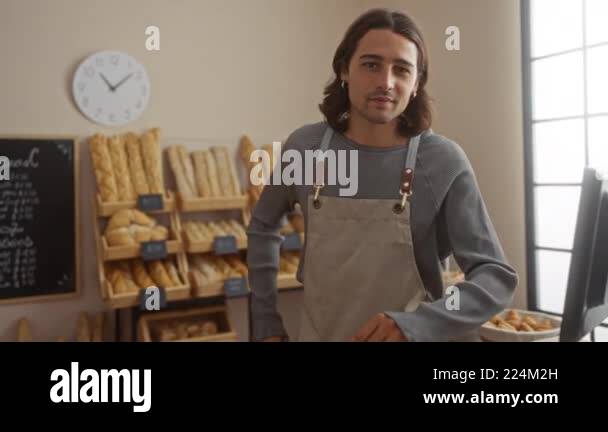 Young man working in a bakery shop with shelves of fresh bread behind ...
