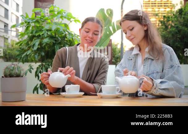 Two young women enjoying tea outdoors, smiling and bonding while ...