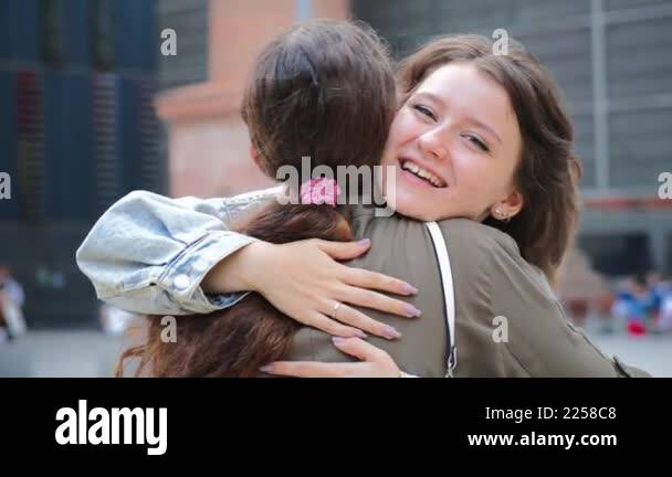 Young woman smiling warmly while hugging a friend outdoors in an urban ...