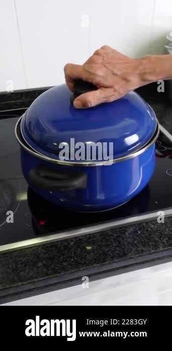 Vertical shot of hand of female chef lifting the lid of a large blue ...