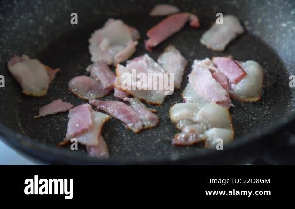 Pieces of bacon are fried in a non-stick marble frying pan close up. 4K ...