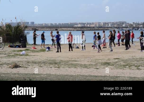 Energetic Group Fitness Session on a Sandy Beach with Urban Background ...