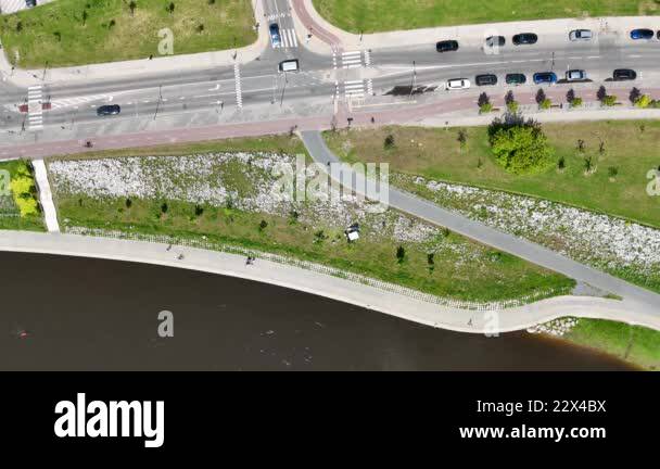 Aerial view of a riverside park with a road, bike path, and parked cars ...