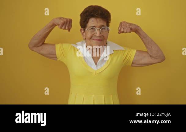 Strong elderly woman in a yellow dress flexing her biceps against a ...