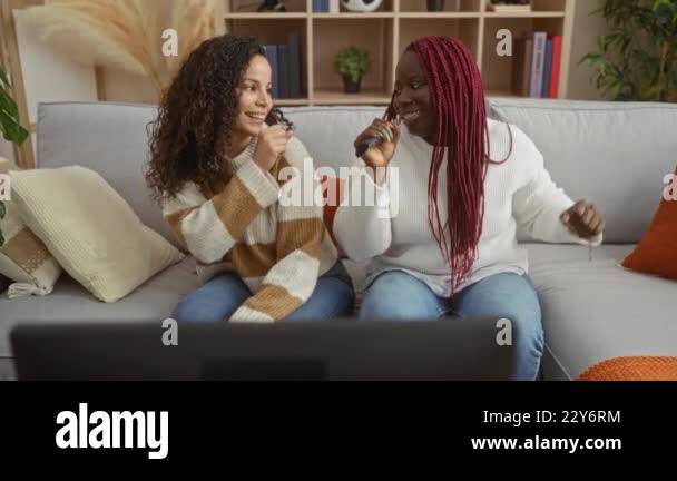 Women friends singing joyfully at home using a remote as a microphone ...