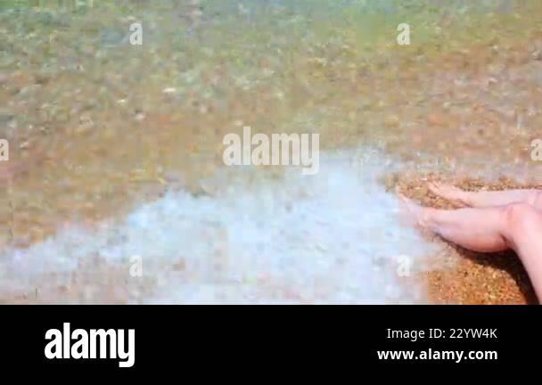 Gentle wave washing over pebble beach with sunlit water and relaxed ...