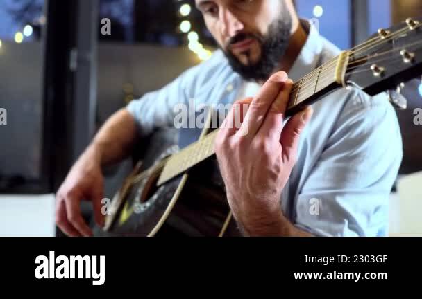 bearded man in shirt plays black acoustic guitar at home, guy musician ...