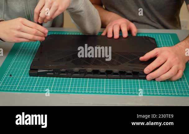Son helping father repair notebook laptop, using screwdriver to open ...