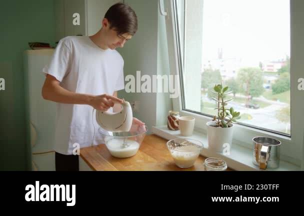 Teen boy whipping cream for cake in mixing bowl. Male teenager using ...