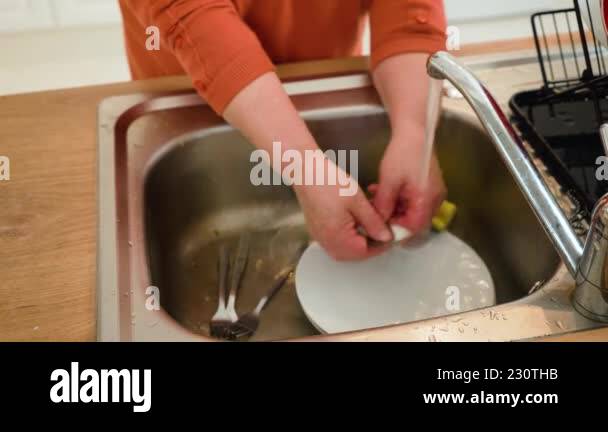 Woman scrubbing dishes in sink. Adult female washing plates with ...