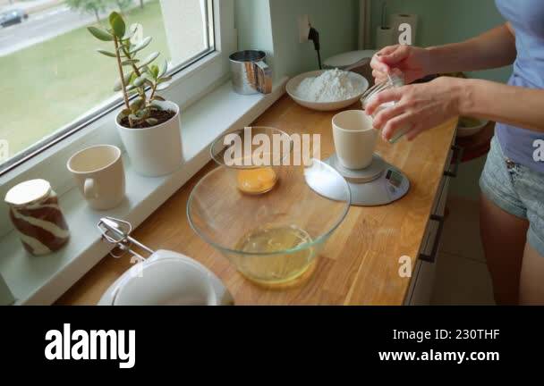 Woman pouring sugar into cup on kitchen scales, preparing ingredients ...
