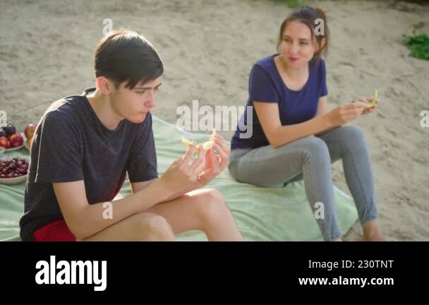 Mother and son eating melon and engaging in light conversation. Woman ...