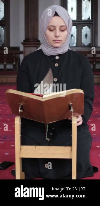 Woman in hijab reciting quran inside mosque, praying al-quran on lectern, muslim reading from ...