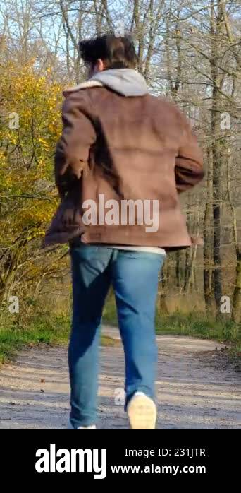 A young man running on the footpath in an autumn forest and trying to ...
