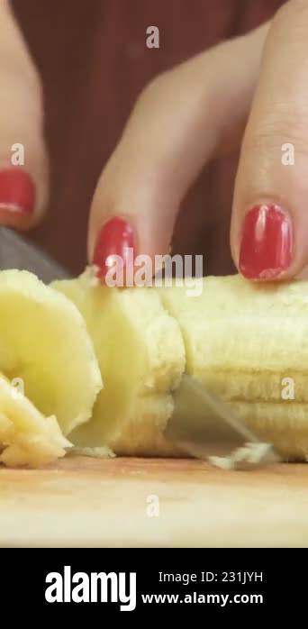 Close-up shot of yellow banana being cut with knife, woman in red nail ...
