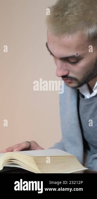 Young man reading a book at his desk indoors, carefully examining the ...