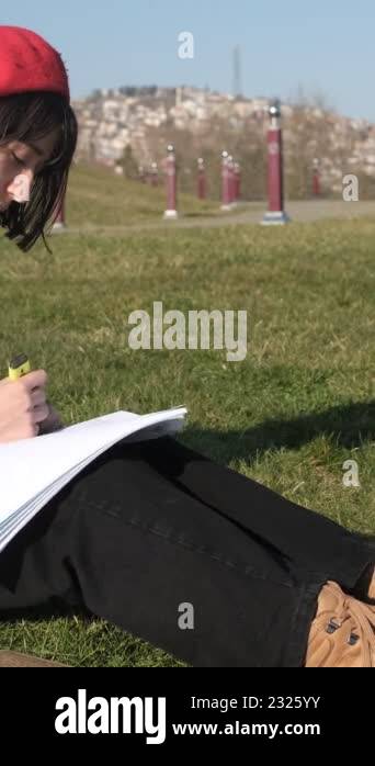 Studying on grass, young beautiful woman checking homework outside ...