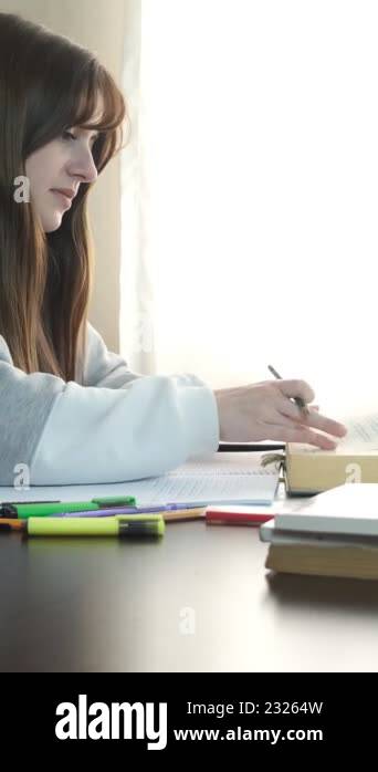 Image of female student studying at desk, taking notes in notebook with ...