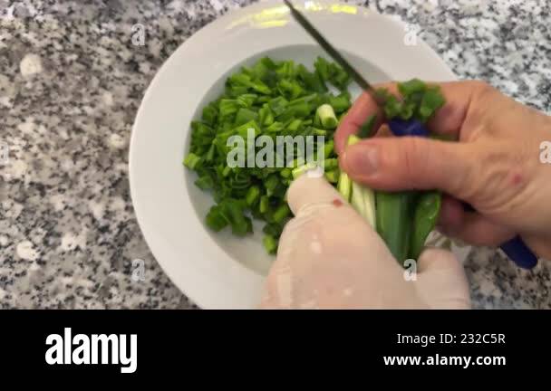 a gloved hand chops the spring onions with a knife on a plate Stock ...
