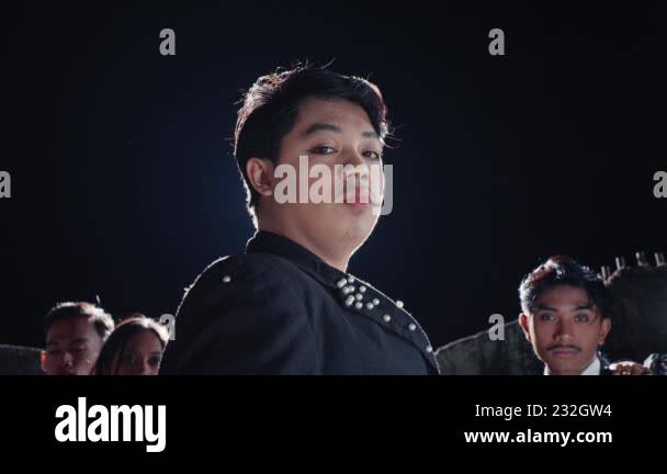 A confident young man in a black outfit with studs, standing in the ...