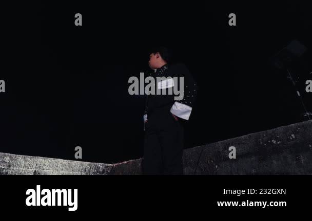 A person standing on a ledge at night, wearing a stylish black outfit ...