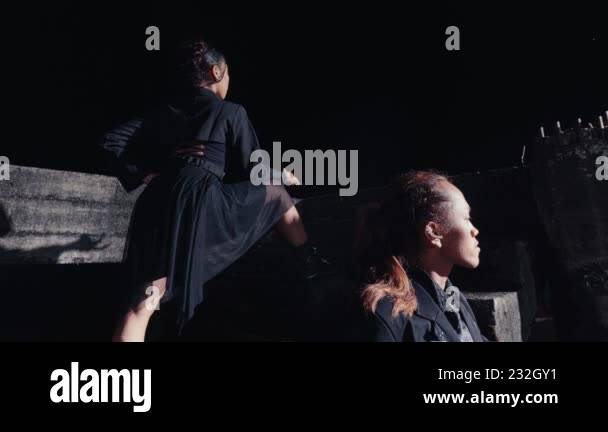 A dramatic scene featuring two models in dark, stylish outfits. One ...