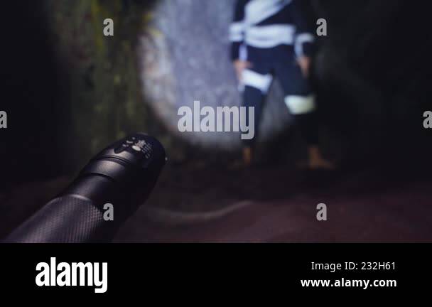 A flashlight beam illuminates a dark, textured wall in a cave or tunnel ...