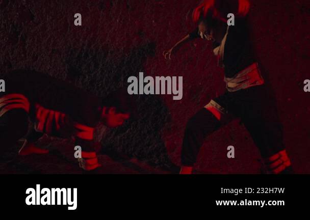 Two figures in dark clothing engage in a dynamic pose against a red ...