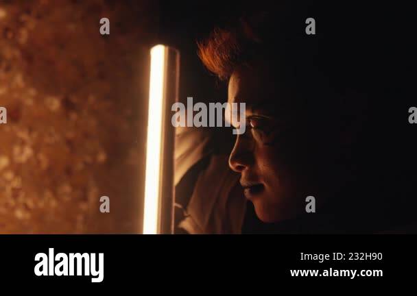 A close-up portrait of a person in low light, with dramatic shadows and ...