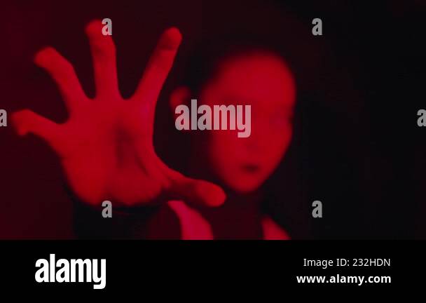 A blurred figure with a hand raised in front, illuminated by red light ...