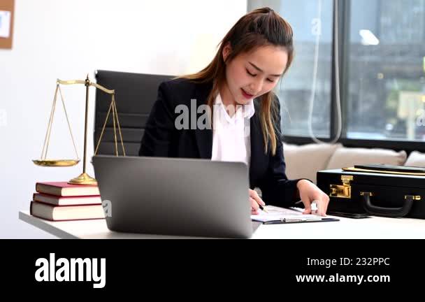 Professional female lawyer working on laptop computer during video chat at a desk, featuring a ...