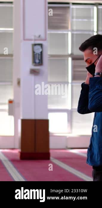 Muslim young man with black health mask on his face praying in mosque ...