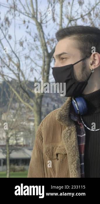 Young man with black health mask on his face standing in the park and ...