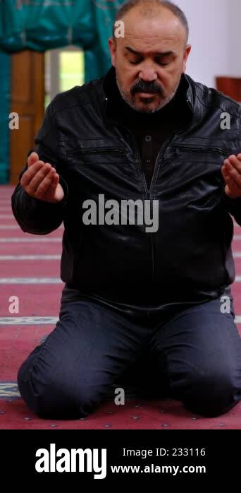 Front shot of mature man sitting in mosque with open hands and praying ...
