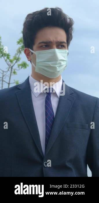 Young man in suit with medical mask on his face talking on the phone ...