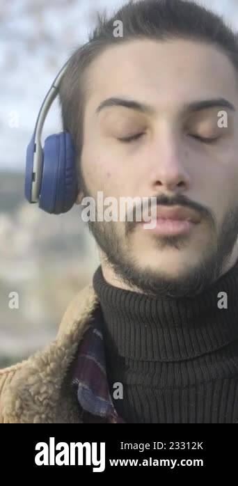 A young bearded man staggering backwards wearing earphones on his neck ...