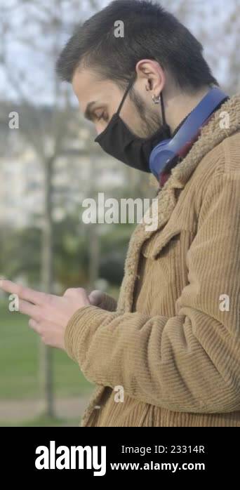 Side view of young man with black medical mask on his face talk with ...