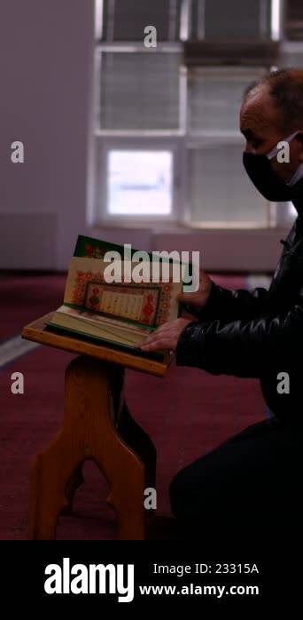 Masked man sitting kneeling in the masjid reading the Quran at the ...